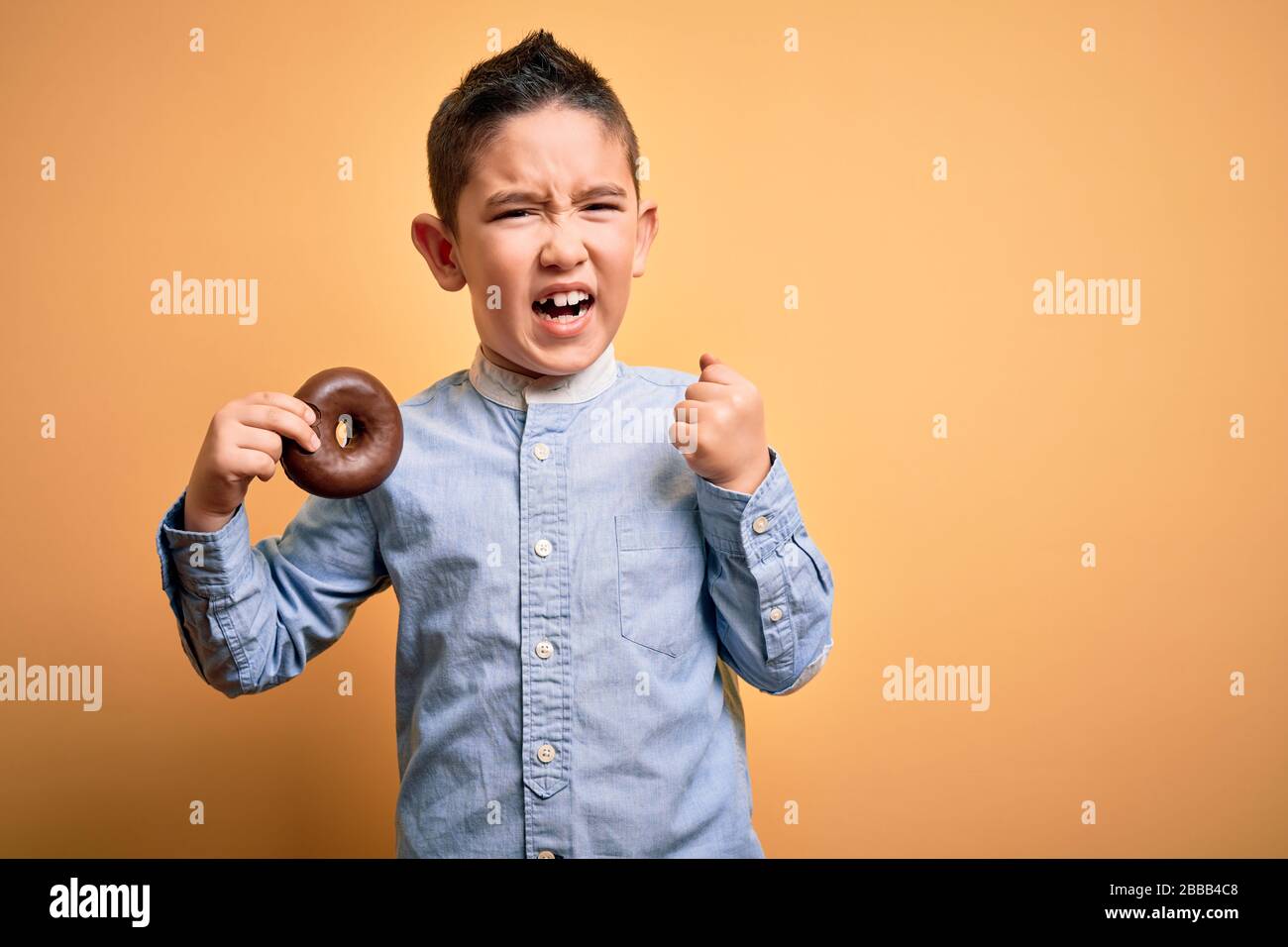 Young little boy kid eating unhealthy chocolate doughnut over isolated ...
