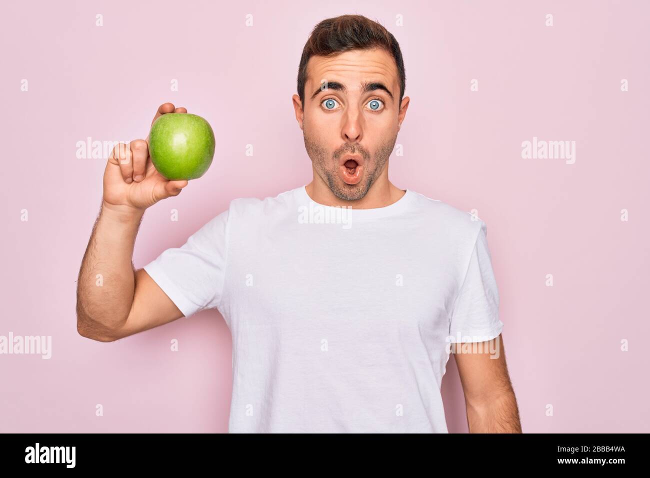 Young handsome man with blue eyes eating healthy green apple over ...