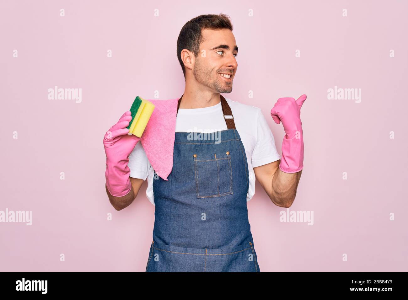 Young cleaner man with blue eyes cleaning wearing apron and gloves ...
