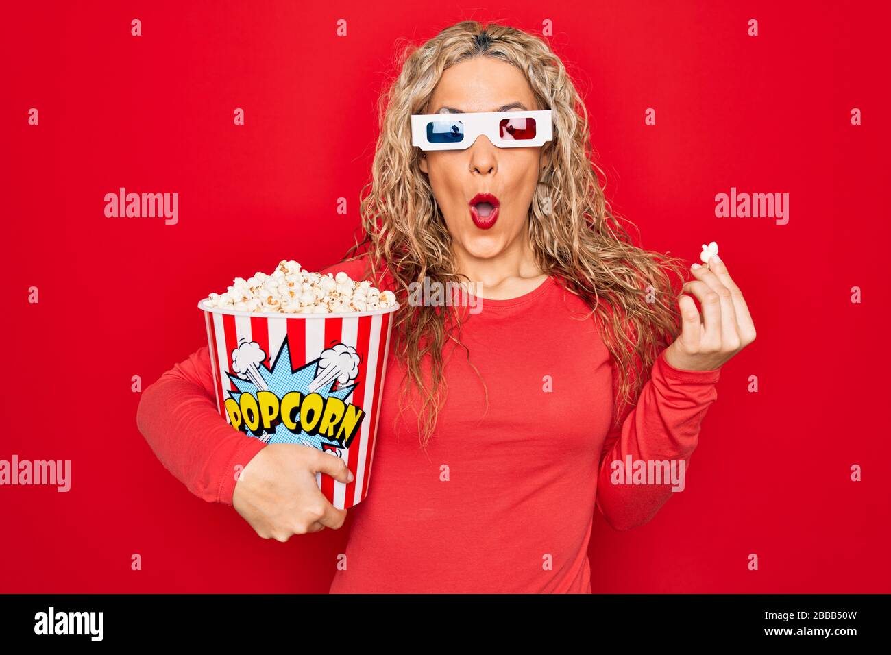 Young beautiful blonde woman watching movie using 3d glasses eating ...