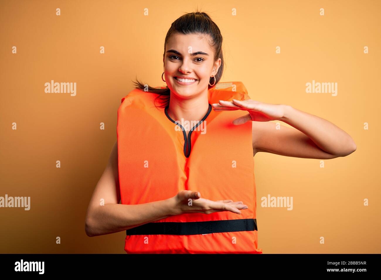 Young beautiful brunette woman wearing orange safe lifejacket over ...