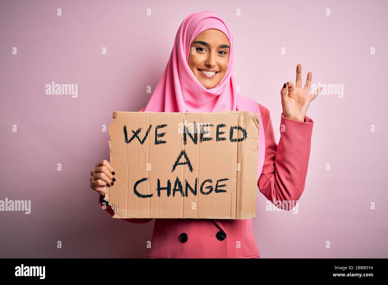 Activist woman wearing pink muslim hijab holding banner with we need a ...