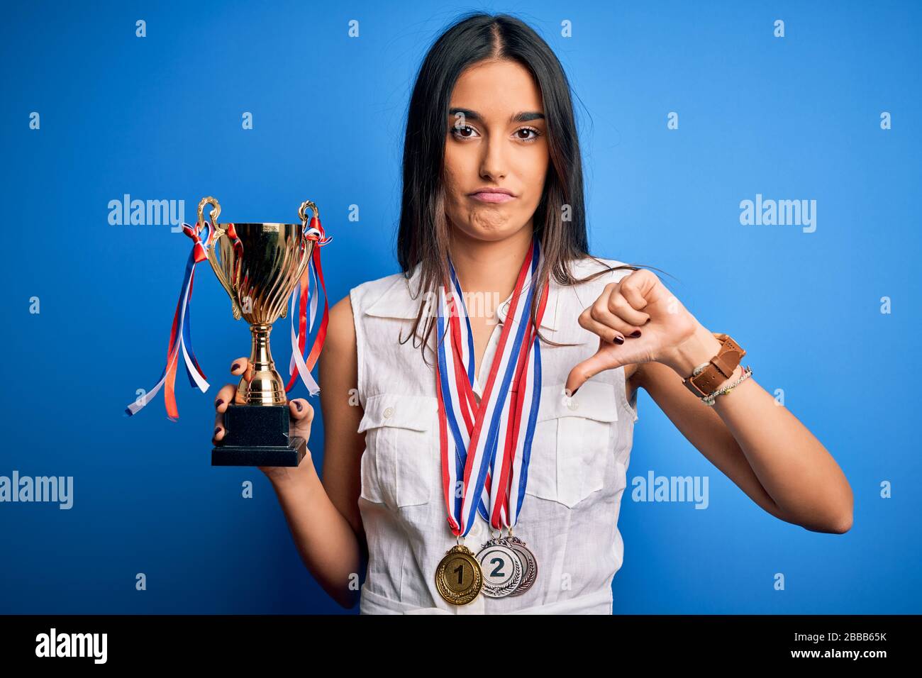 Young beautiful brunette successful woman wearing medals holding trophy ...
