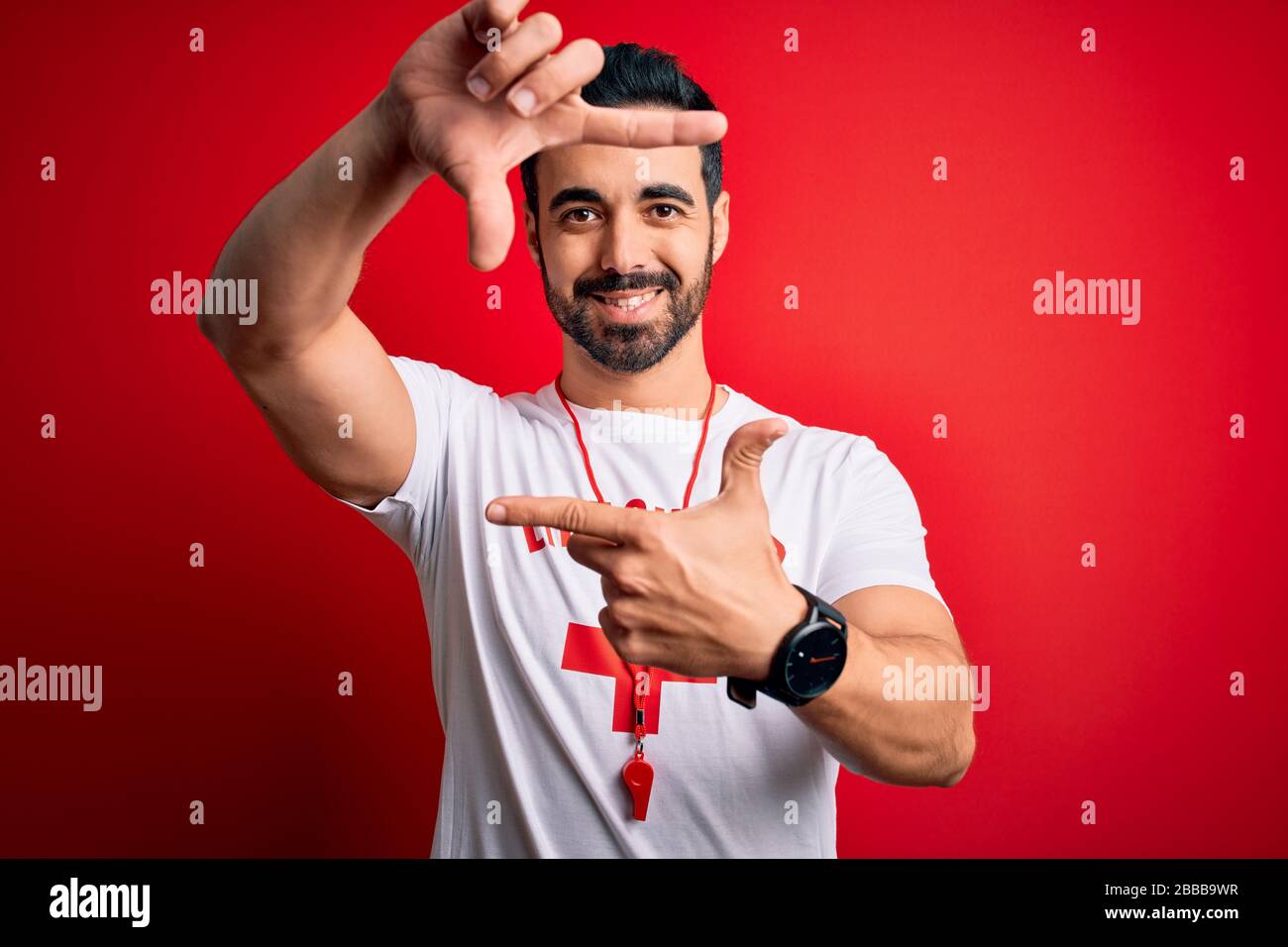 Young handsome lifeguard man with beard wearing whistle over isolated ...