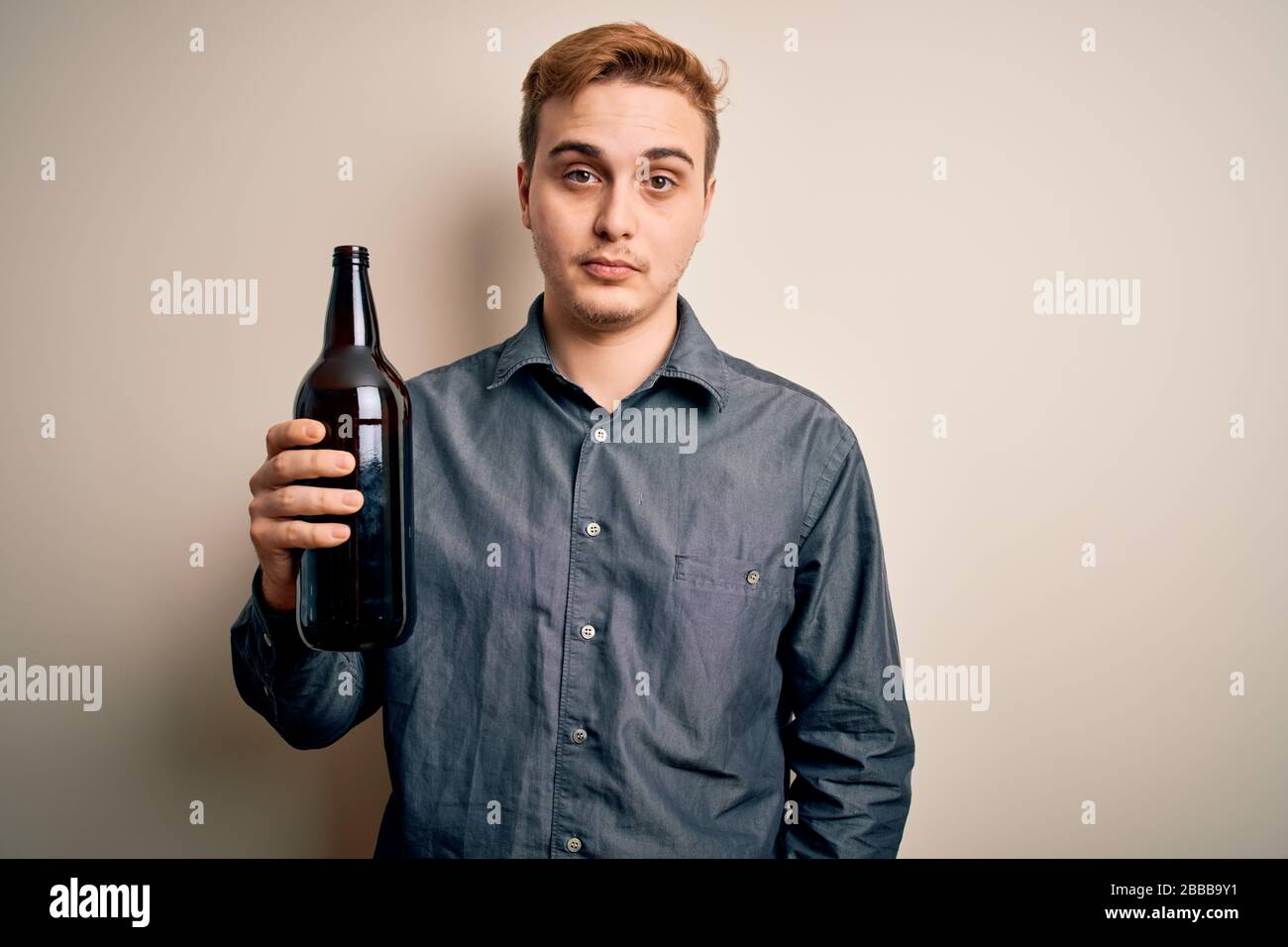 Young handsome redhead man drinking bottle of beer over isolated white ...