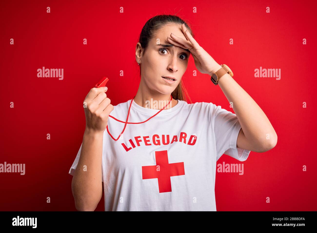 Beautiful lifeguard woman wearing t-shirt with red cross using whistle ...