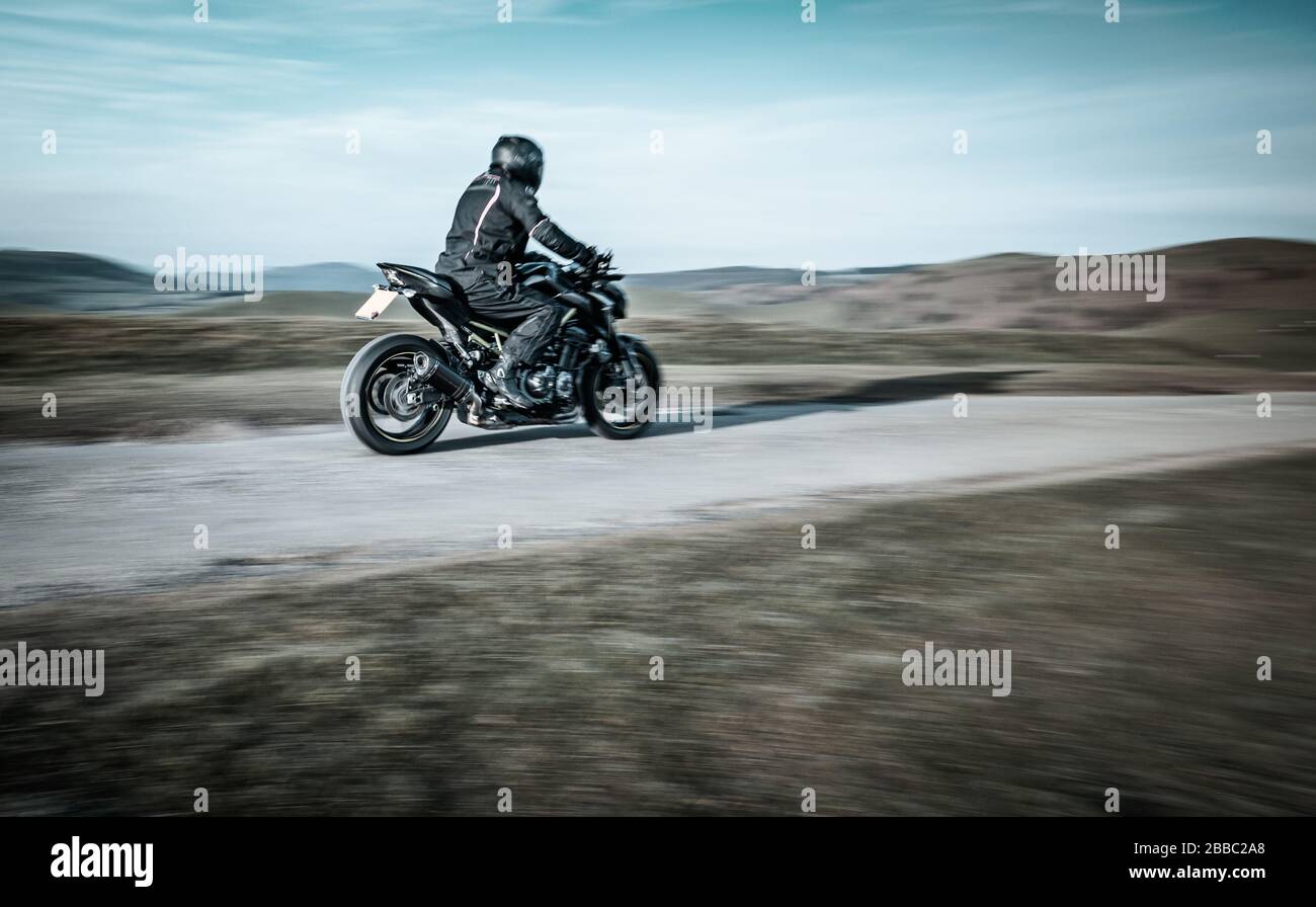 Biker riding sport motorcycle across scenic countryside road - panning ...