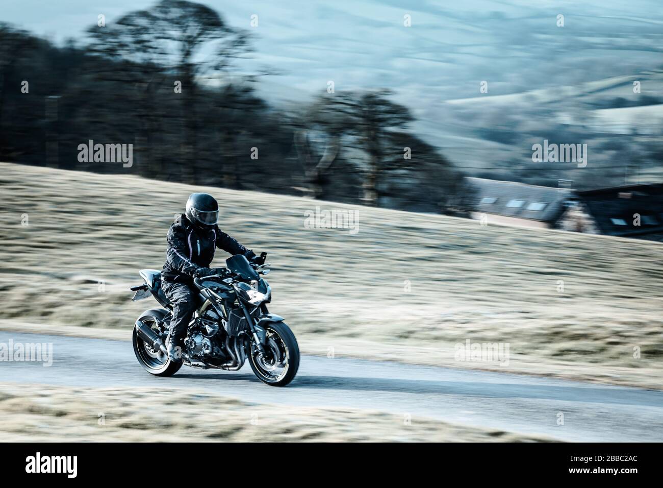 Biker riding sport motorcycle across scenic countryside road - panning ...