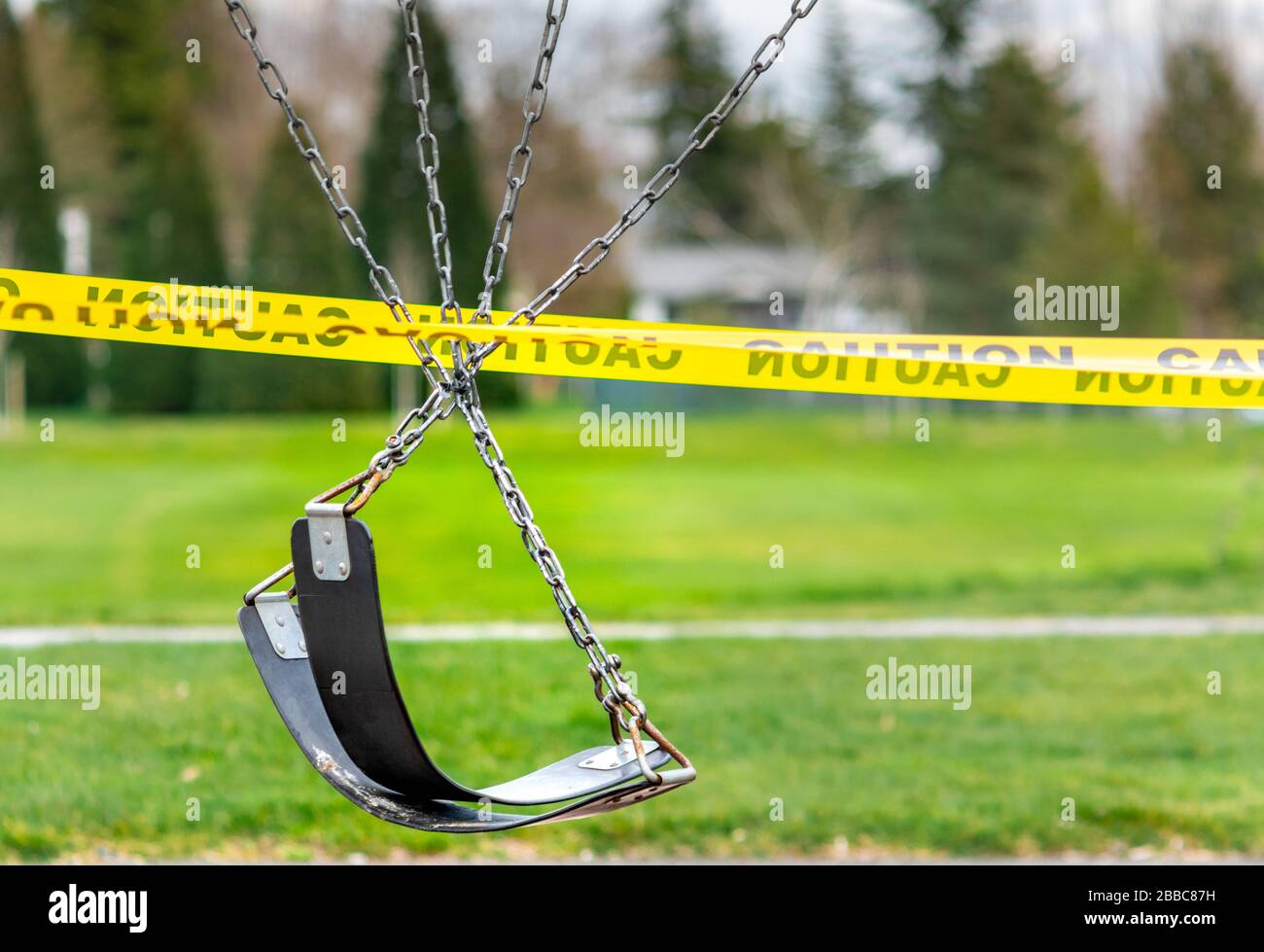 Black rubber swings on chains in closed public playground surrounded by ...