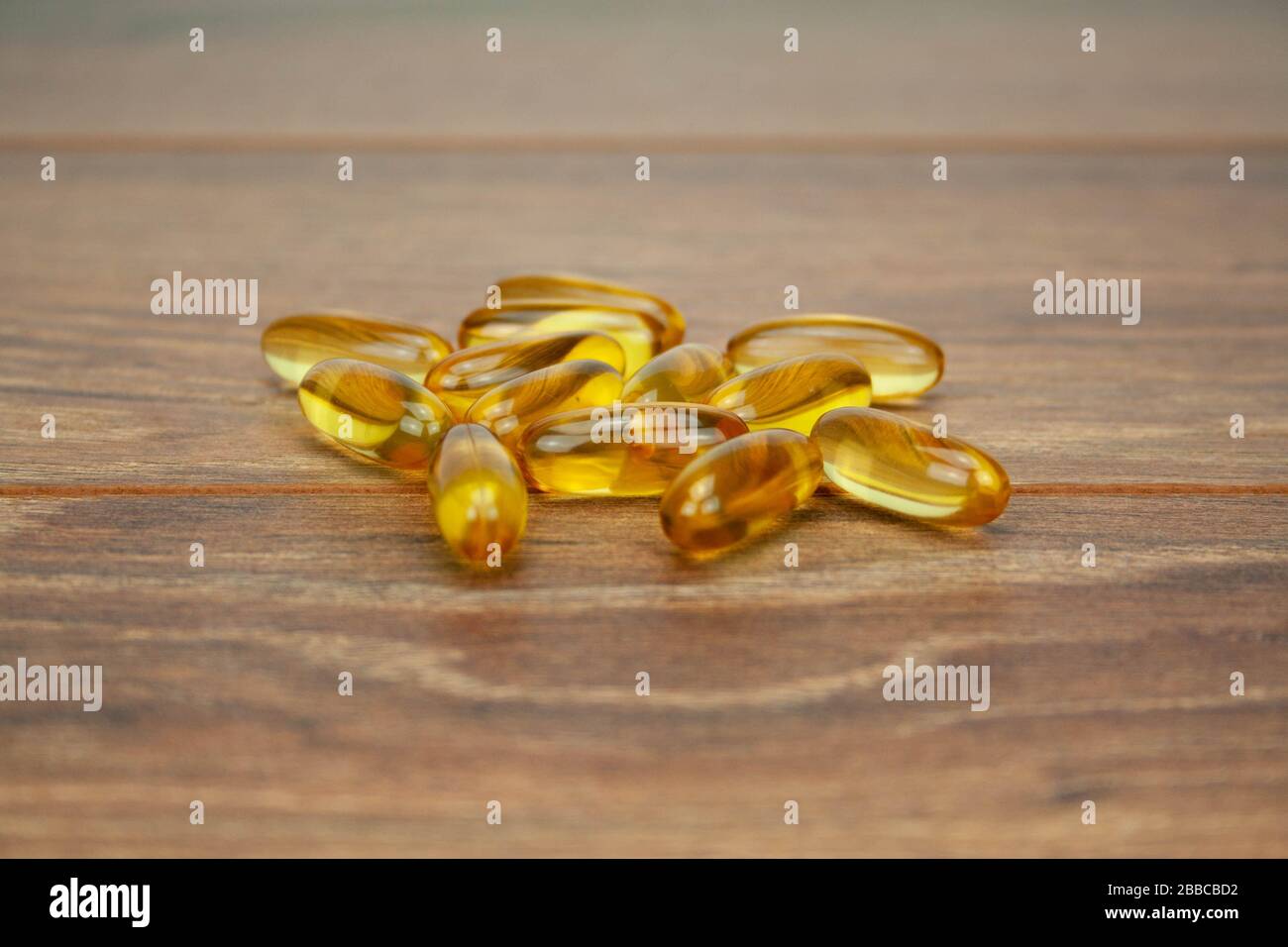 Many transparent oval tablets with oil inside on a wood background ...
