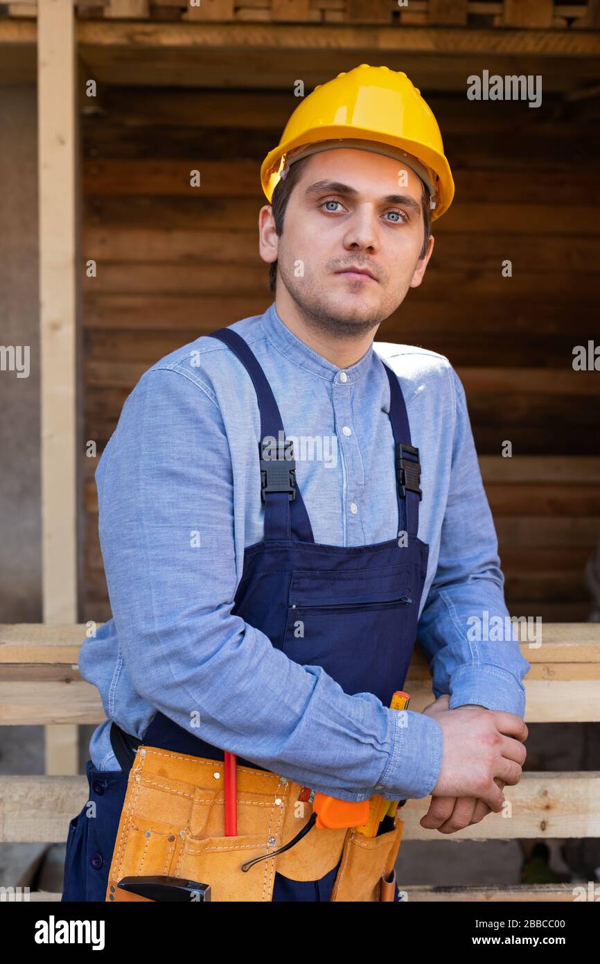 Portrait of a confident young workman wearing yellow helmet, blue ...