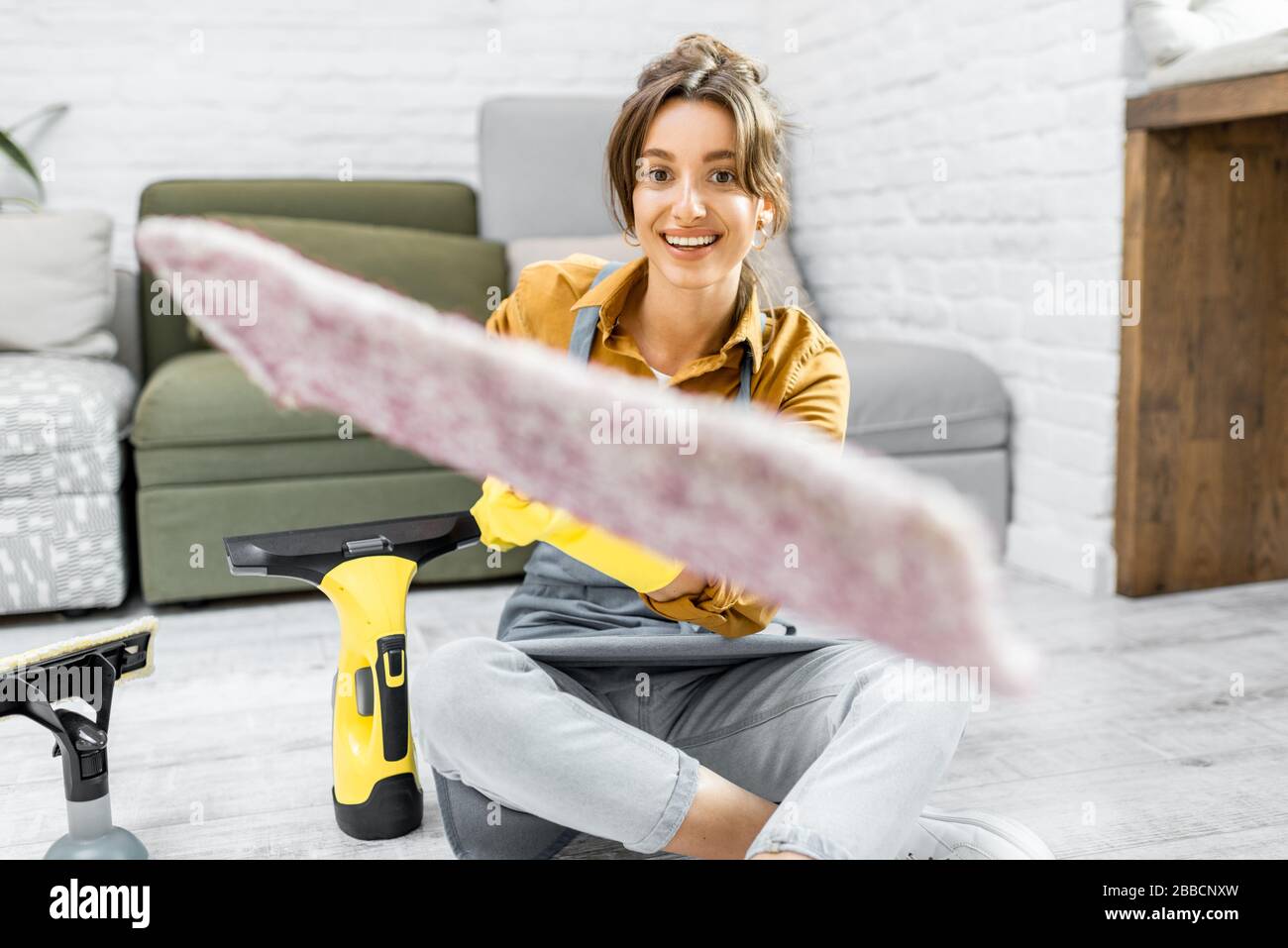 Portrait of a joyful woman as a housewife, pushing forward mop, while ...