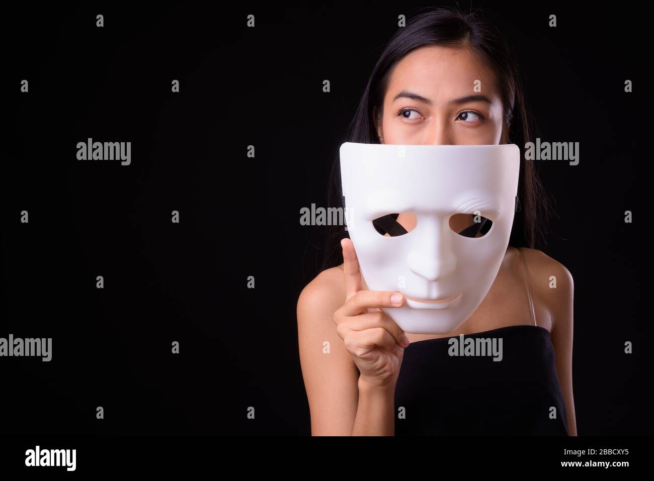 Face of young beautiful Asian woman thinking while holding mask Stock ...