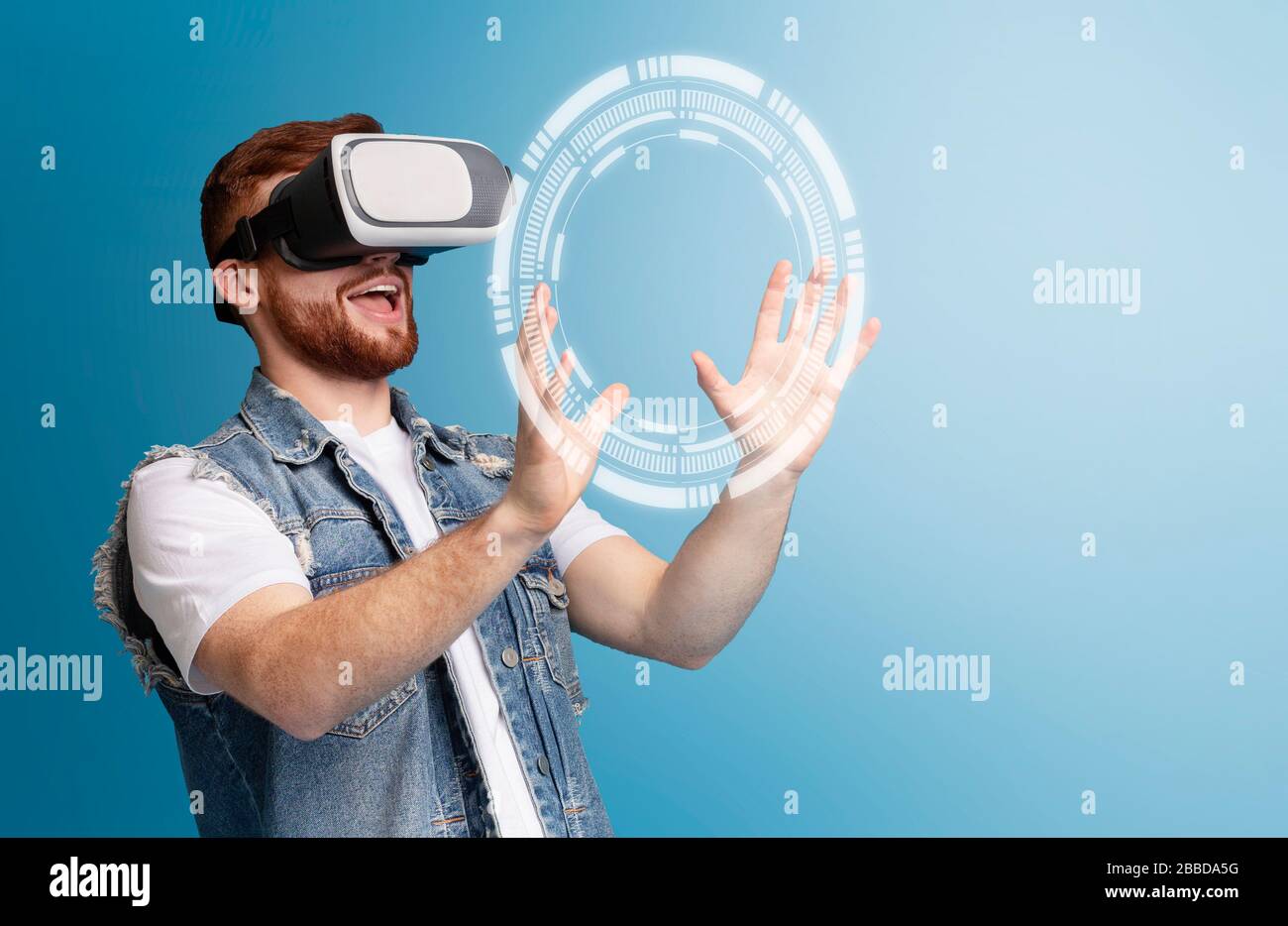 Happy young guy touching virtual screen in VR headset on blue ...