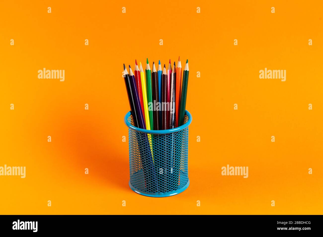 blue metal bucket with colored pencils for office on an orange ...