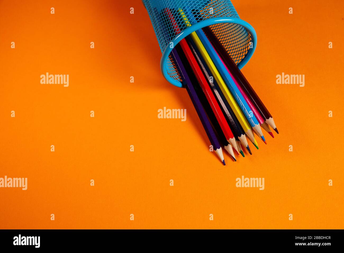 blue metal bucket with colored pencils for office on an orange ...