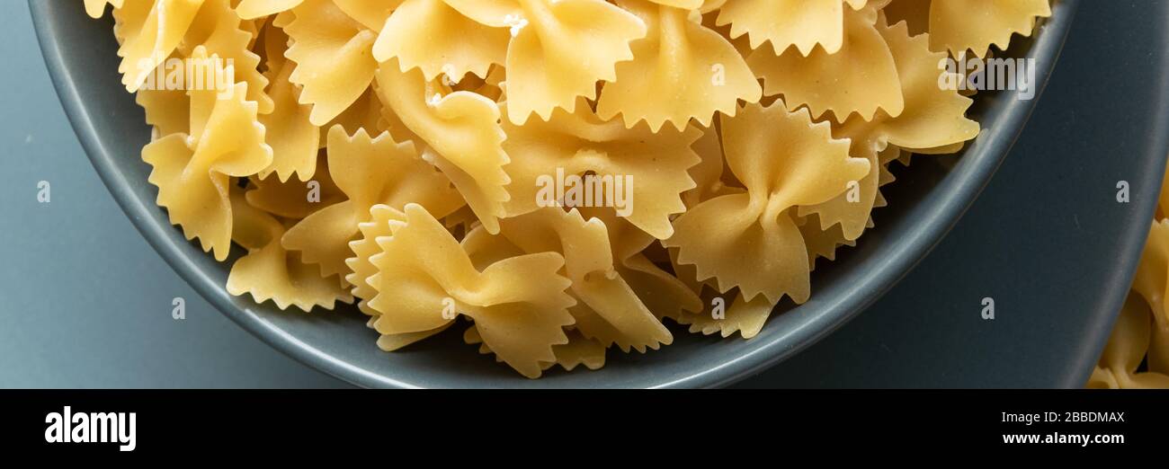 Food background - dry farfalle pasta on grey plate, whole wheat uncooked ingredient, space for ...