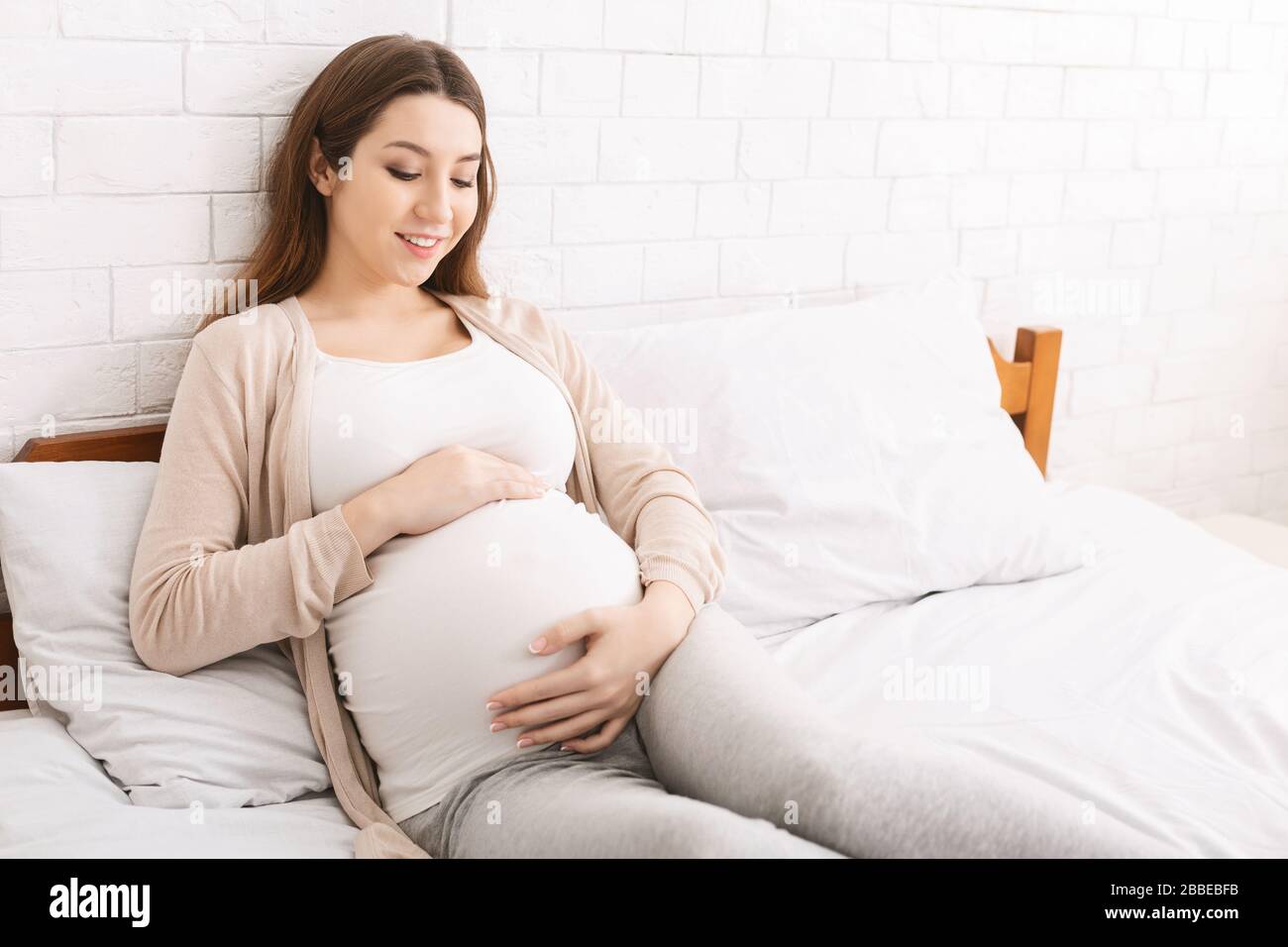 Young expectant woman touching her belly in bed Stock Photo - Alamy