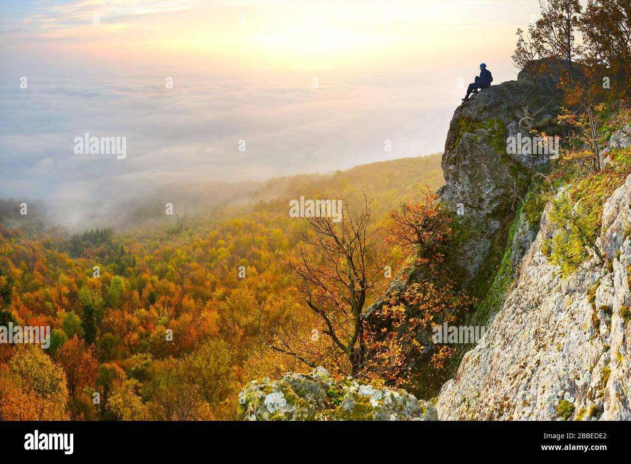Alone Man sitting on the top of the rock under the mist, sunrise sky ...