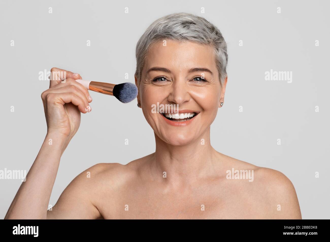 Beautiful smiling middle-aged woman doing makeup, applying blush to her ...