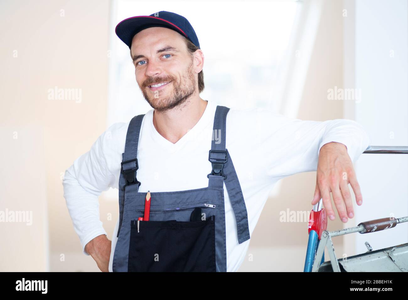 attractive, friendly smiling craftsman in work clothes and with tools ...