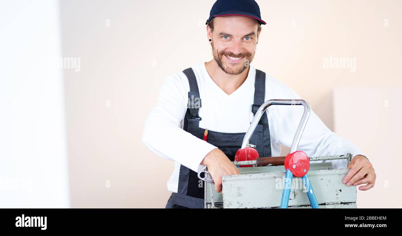 attractive, friendly smiling craftsman in work clothes and with tools ...