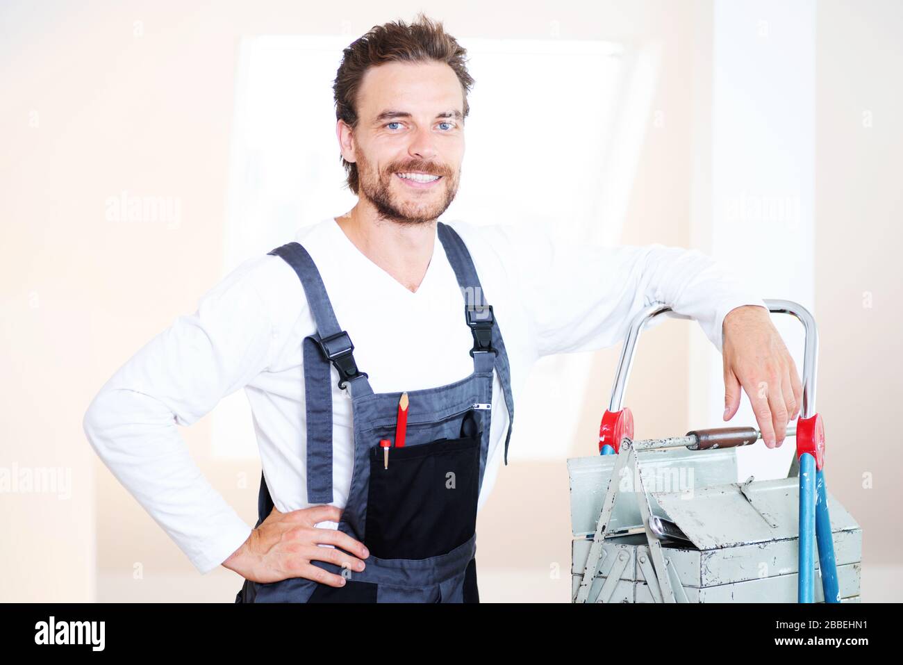 attractive, friendly smiling craftsman in work clothes and with tools ...