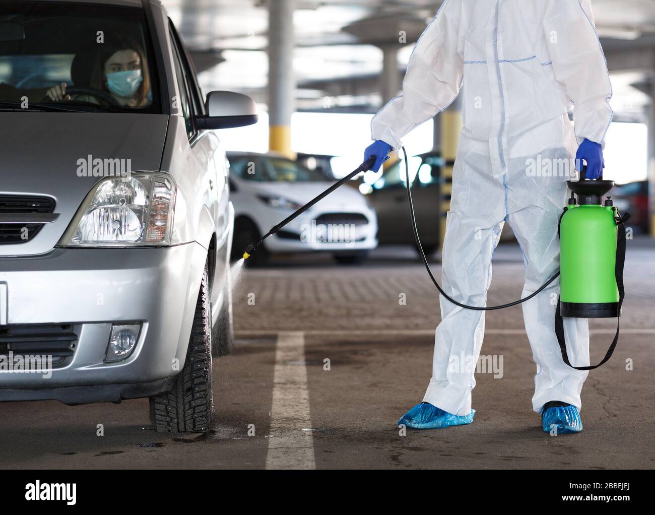 Unrecognizable person disinfecting car with spray with woman inside ...