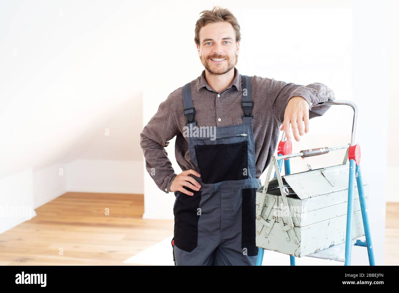 attractive, friendly smiling craftsman in work clothes and with tools ...