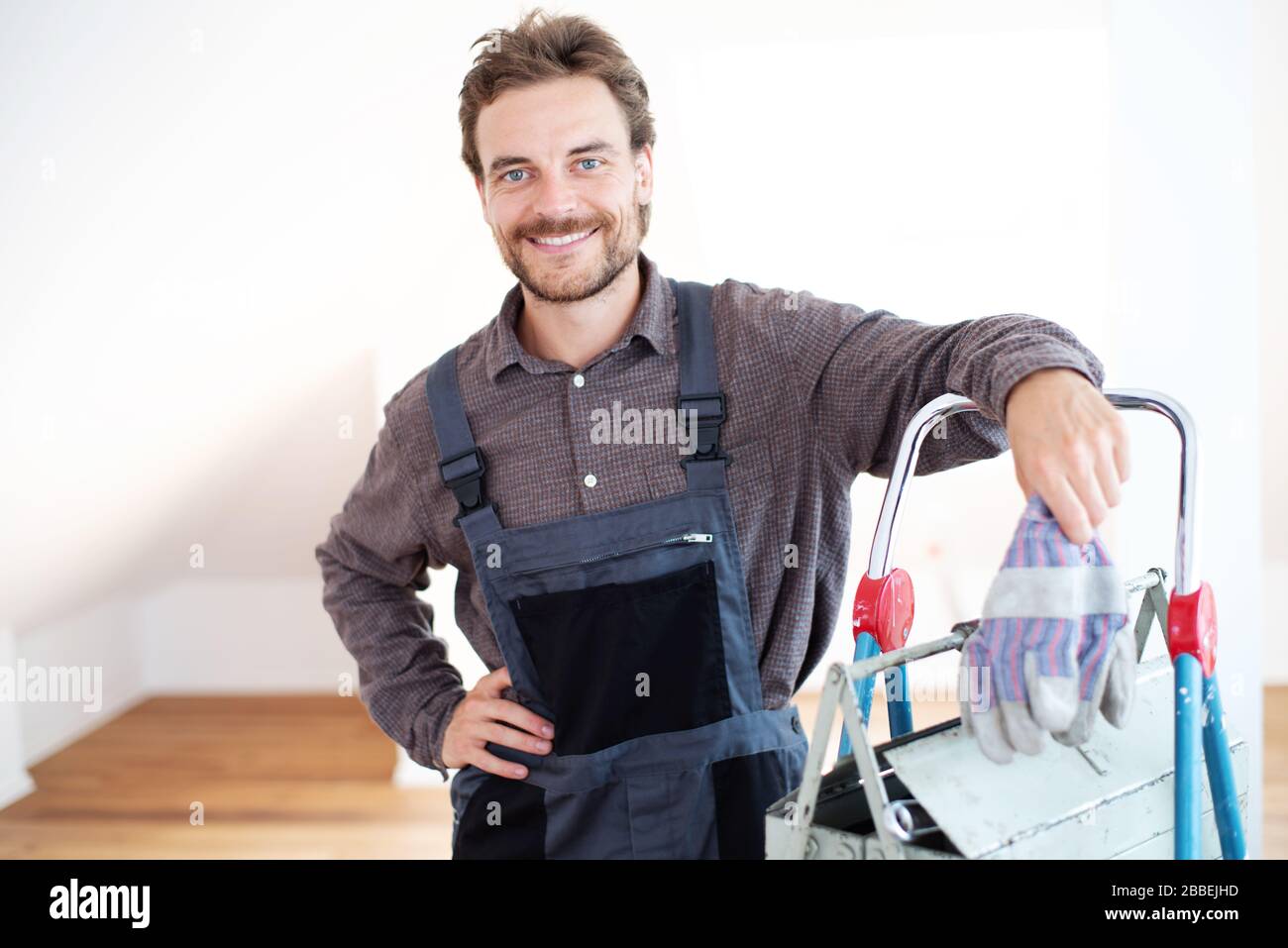 attractive, friendly smiling craftsman in work clothes and with tools ...