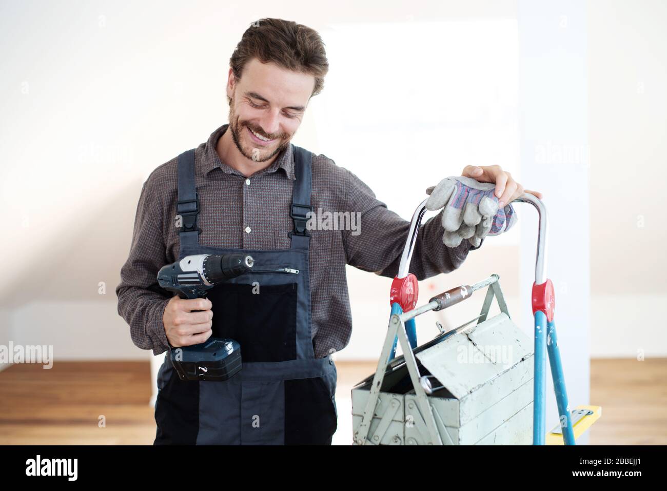 attractive, friendly smiling craftsman in work clothes and with tools ...