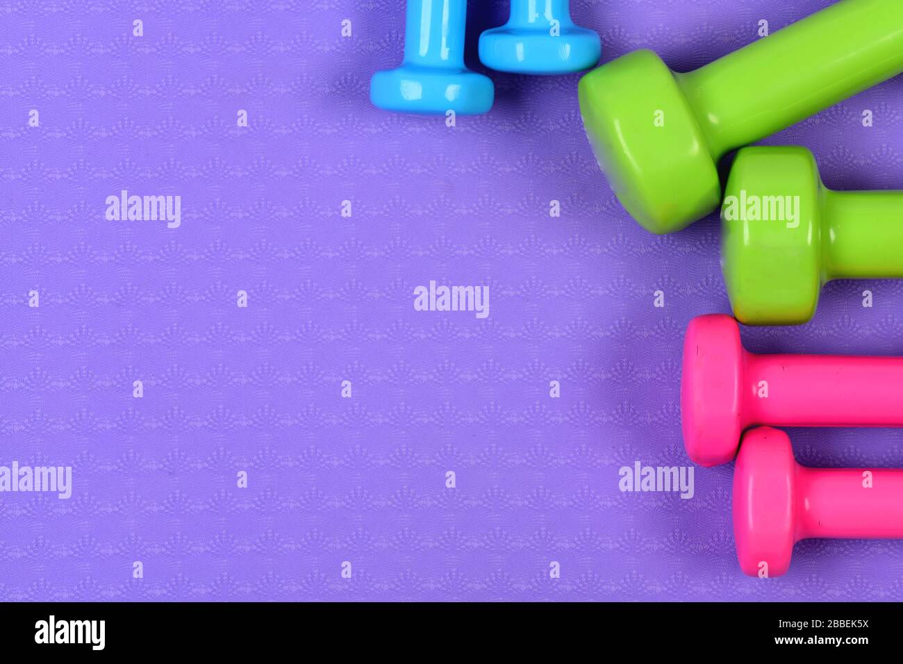 Dumbbells made of pink, green and blue plastic on purple texture ...