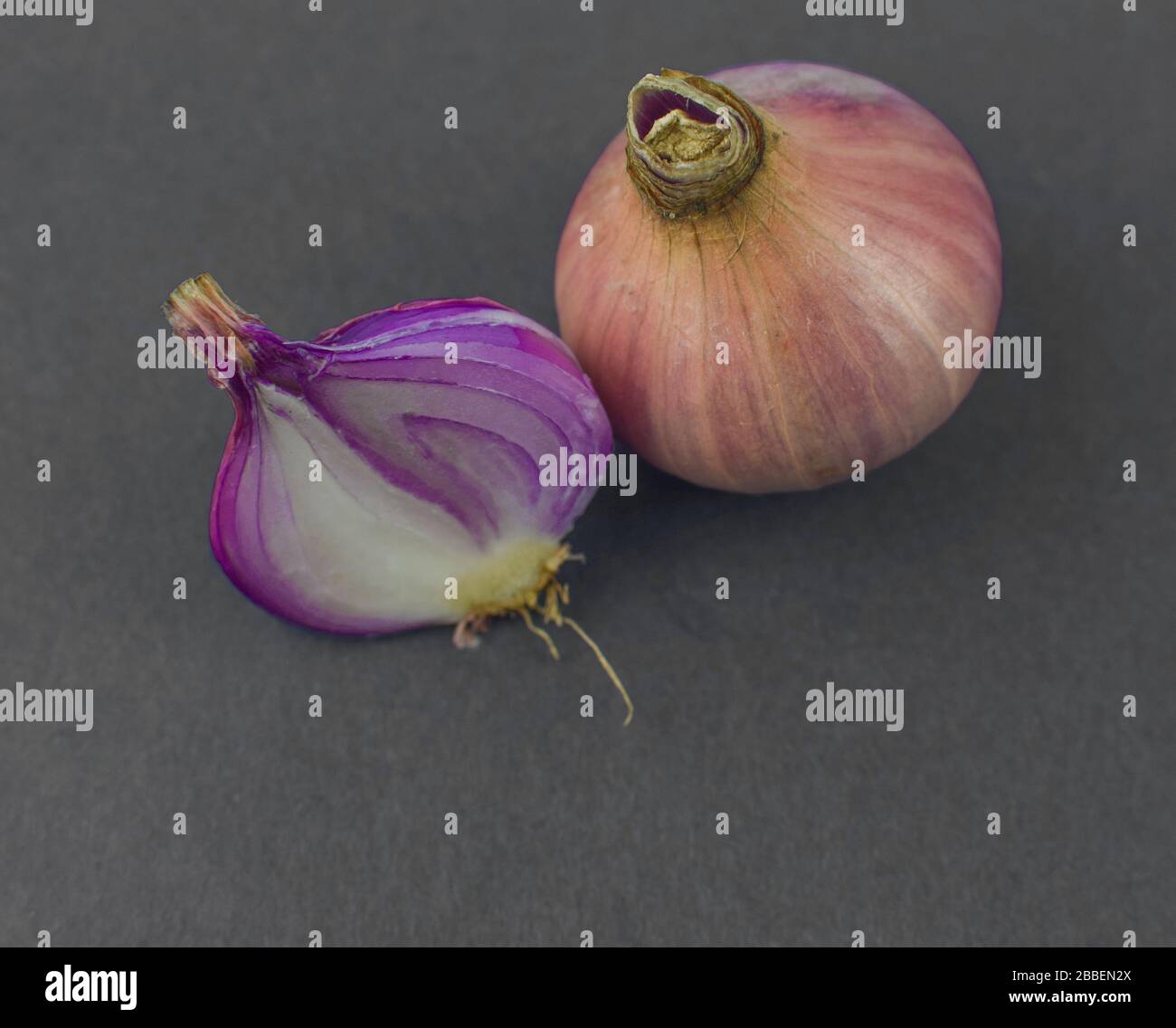 A half peeled pink colored onion placed beside a medium sized unpeeled ...