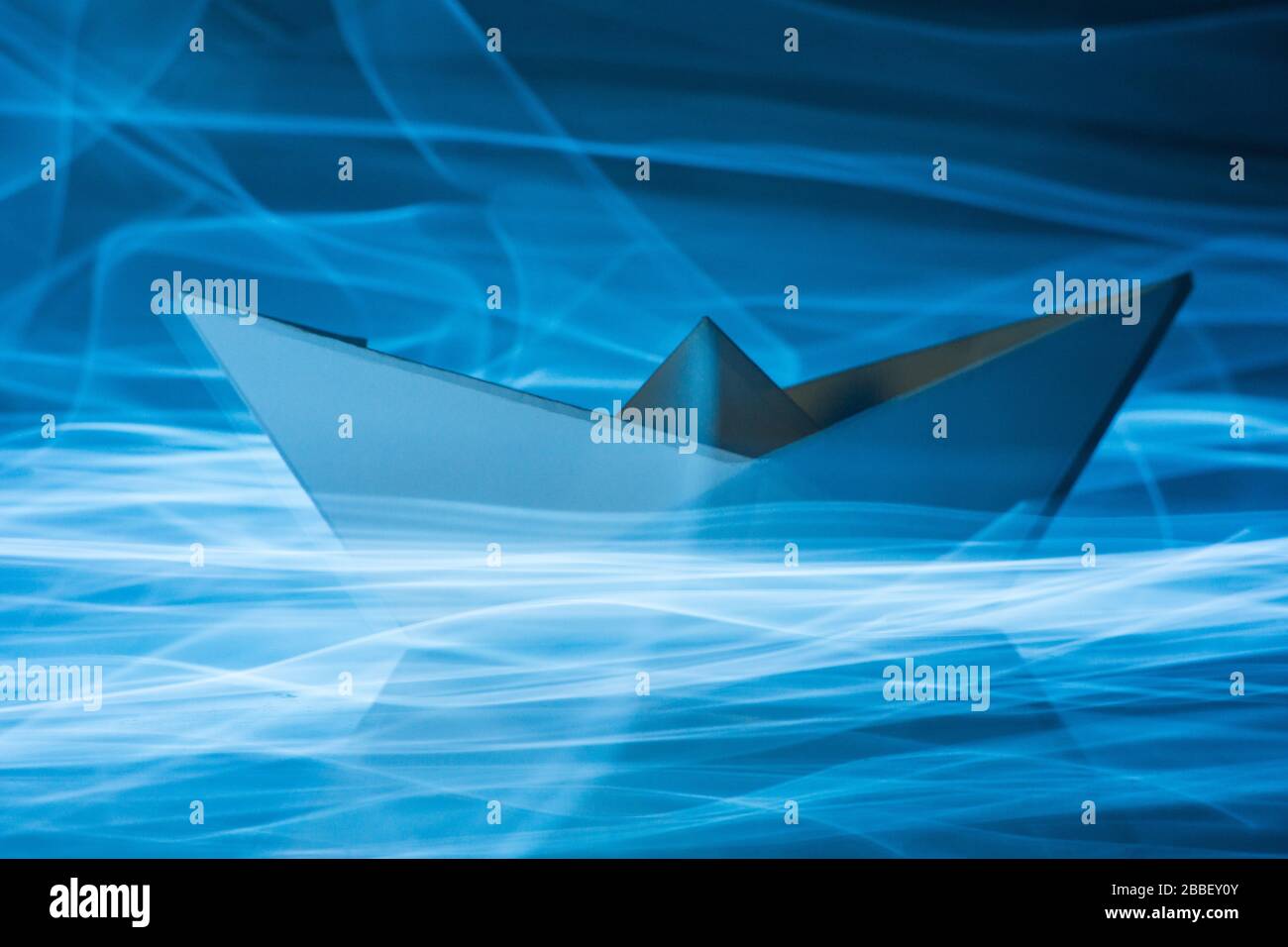 Paper boat splitting blue light trails symbolizing waves in the sea ...