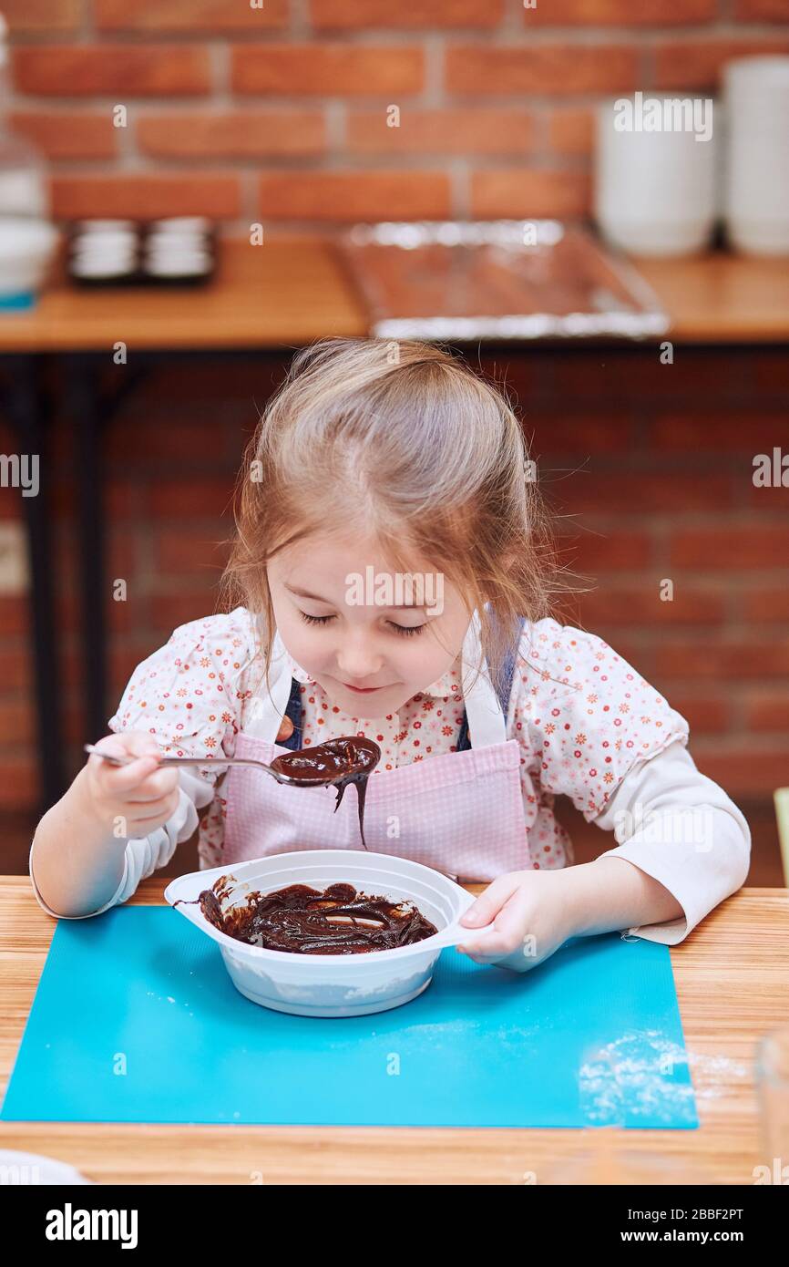 Little girl smelling the melted chocolate and cocoa. Kid taking part in ...