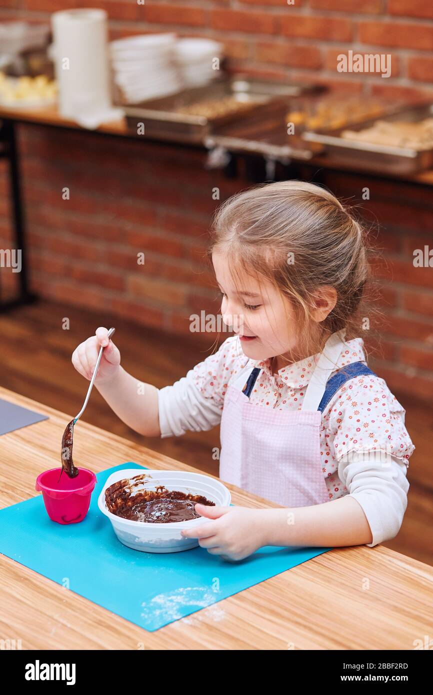 Little girl putting the melted chocolate and cocoa to cupcake. Kid ...