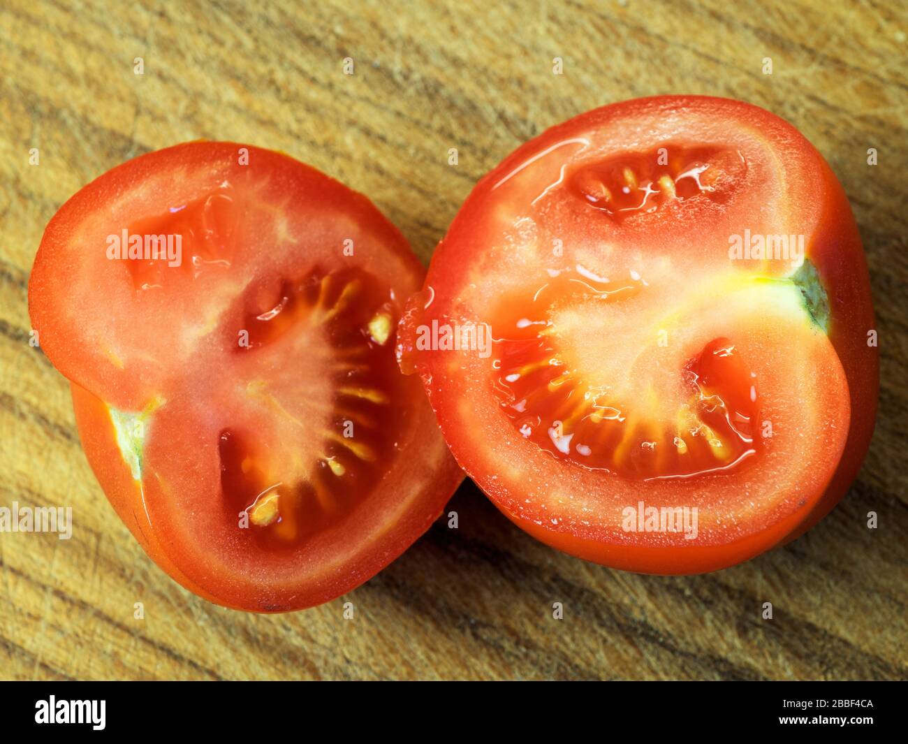 A tomato cut in half on a wooden chopping board Stock Photo - Alamy