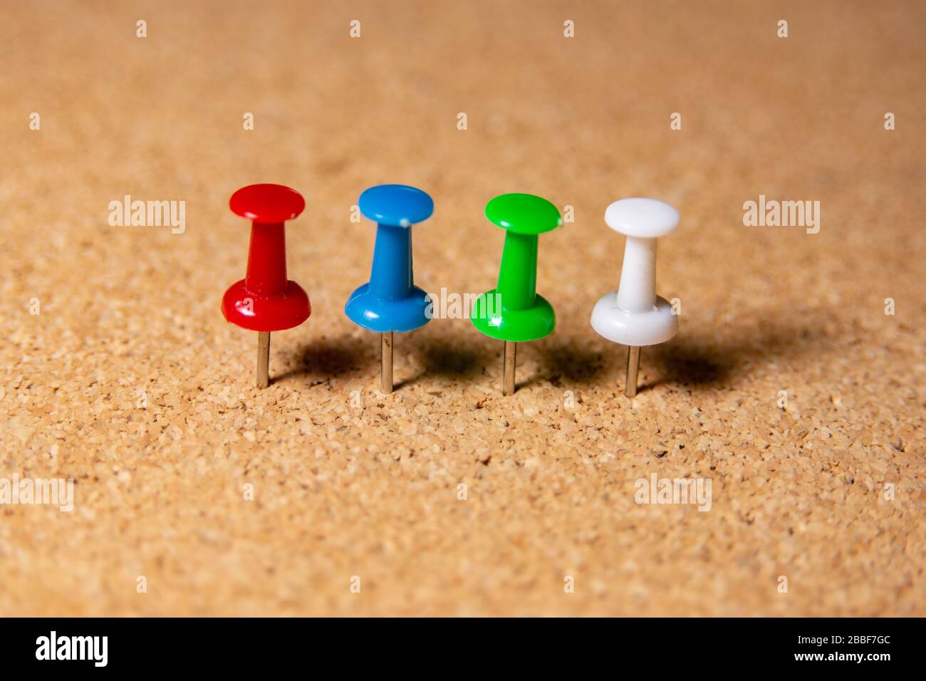 4 colourful pins stuck in the row in cork board Stock Photo - Alamy