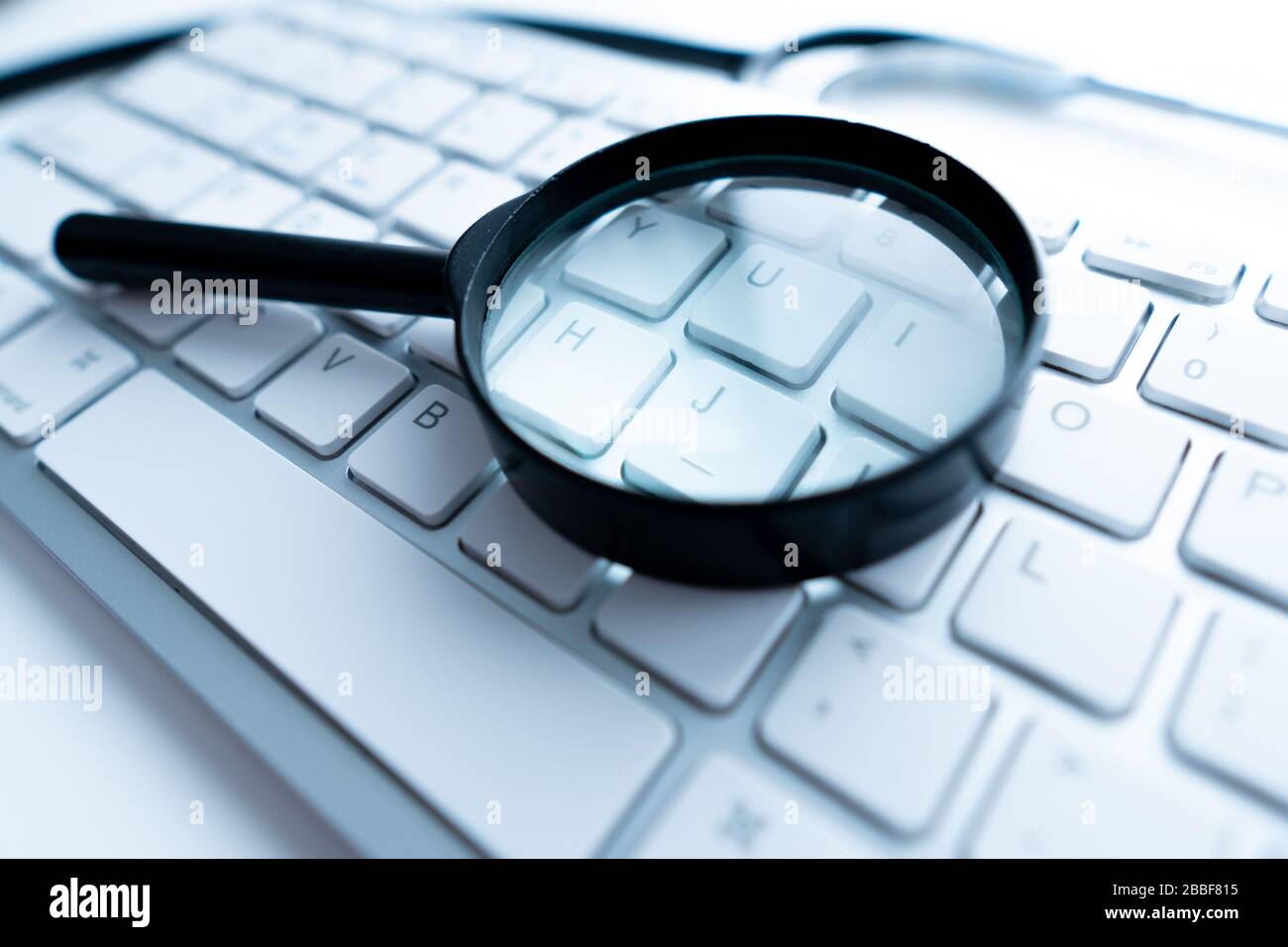 Magnifying glass lies on white keyboard on desk in office table ...
