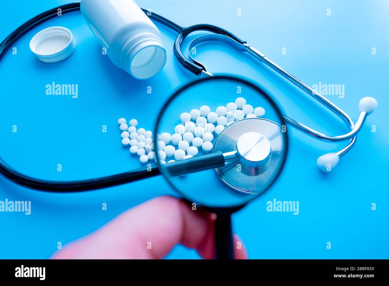 The doctor holds a magnifying glass to see the white pill to treat the ...