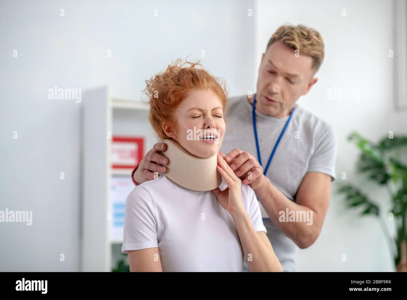 Male physiotherapist examining neck fixator, female patient frowning ...