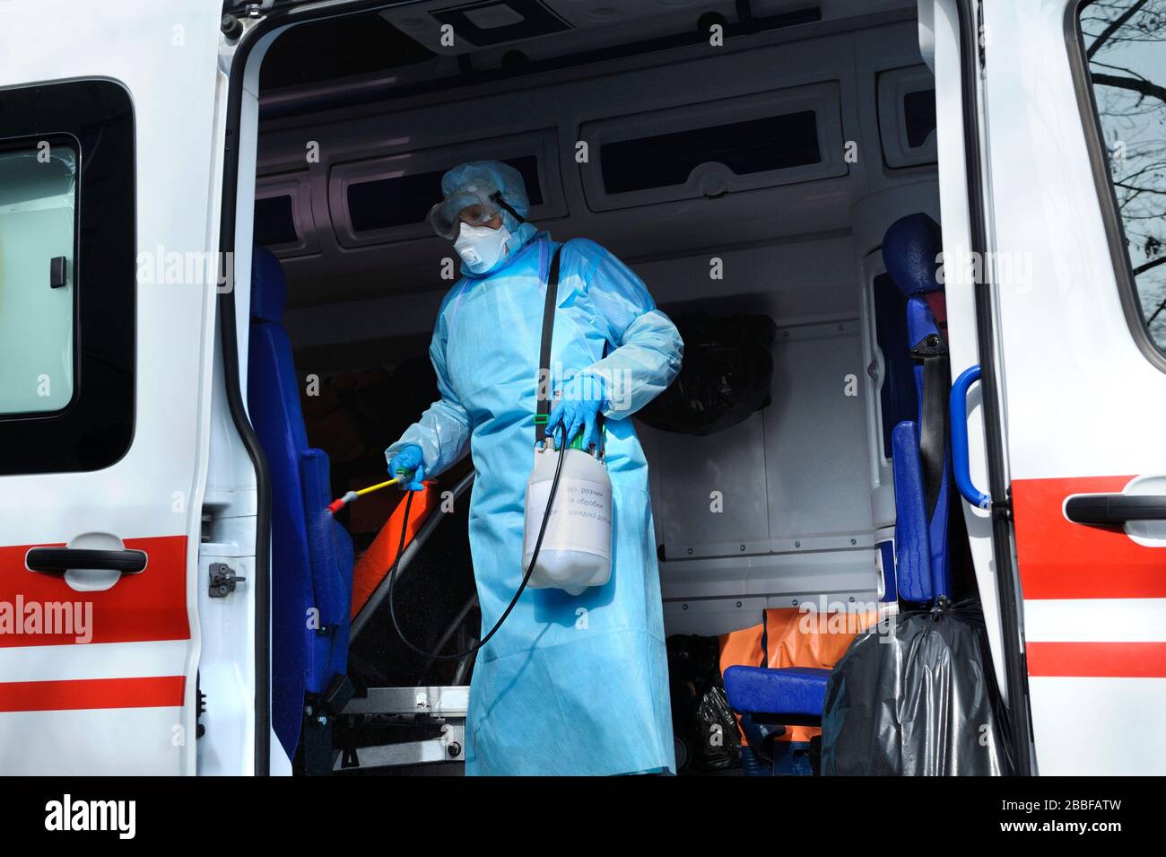 Paramedic in protective mask and costume disinfecting the ambulance car ...