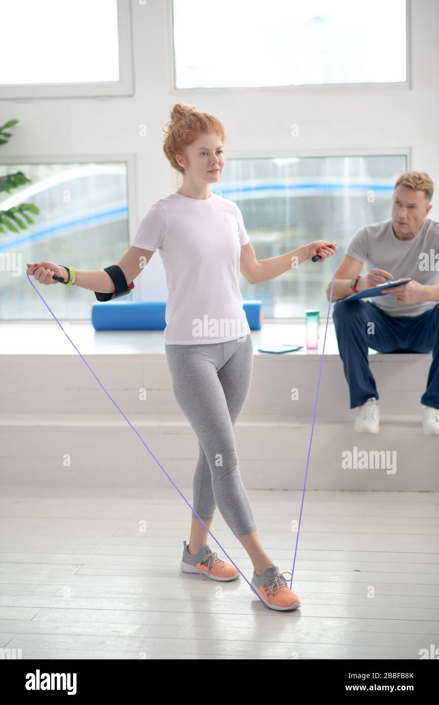 Female patient walking with jump rope, male physiotherapist watching ...
