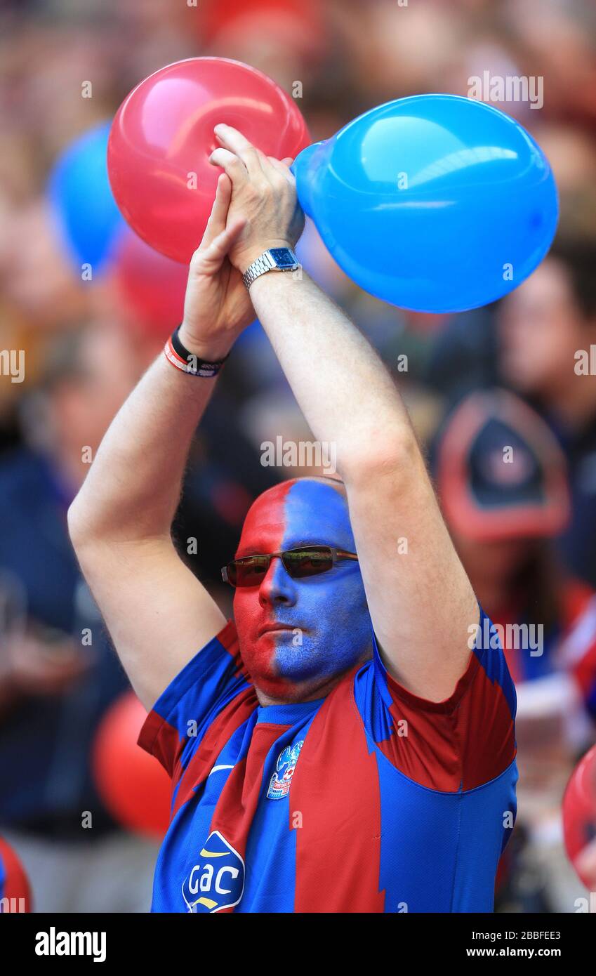 A Crystal Palace fan wearing face paint holds balloons in the stands ...