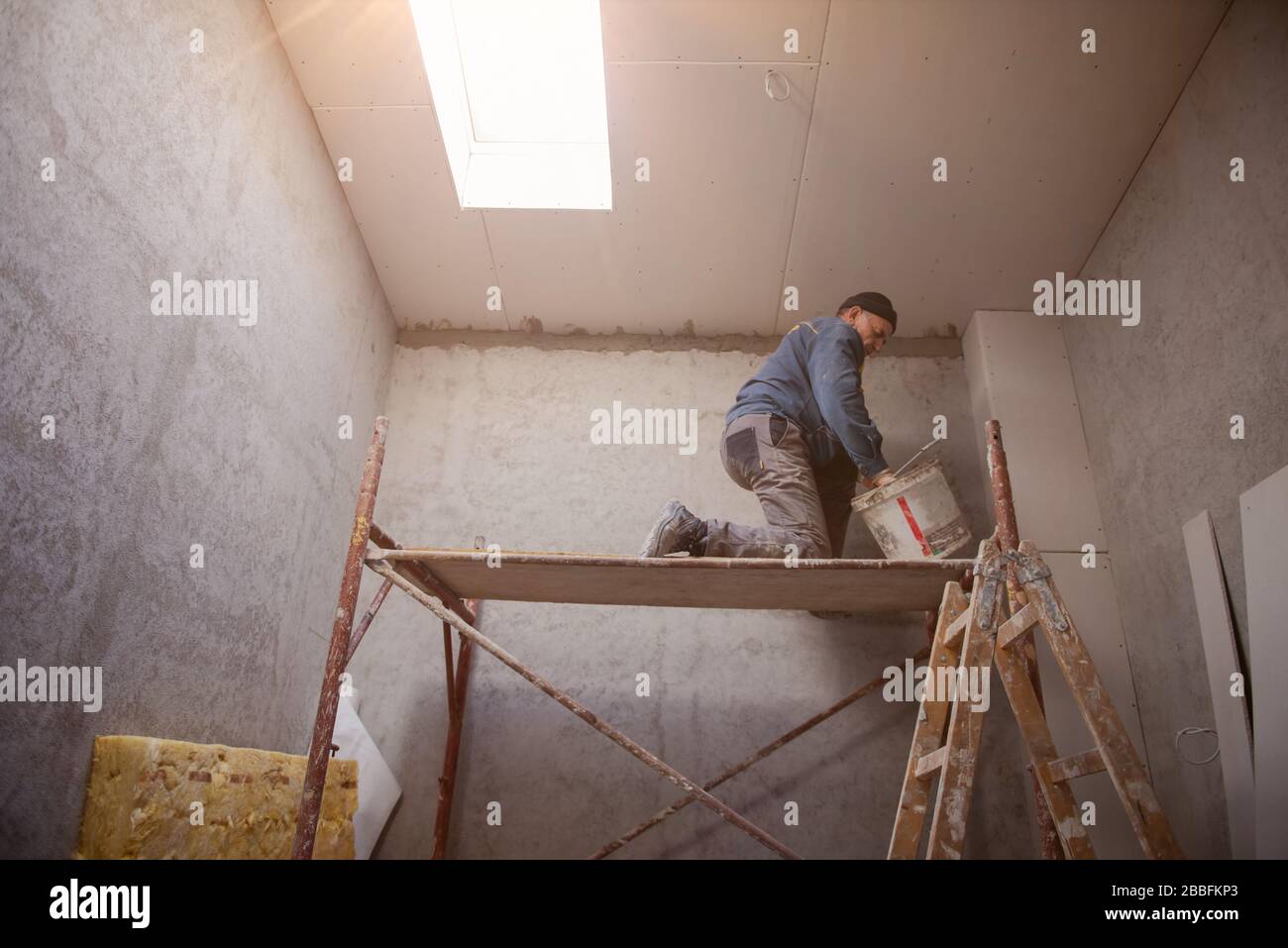 young professional construction worker using scaffold while plastering ...