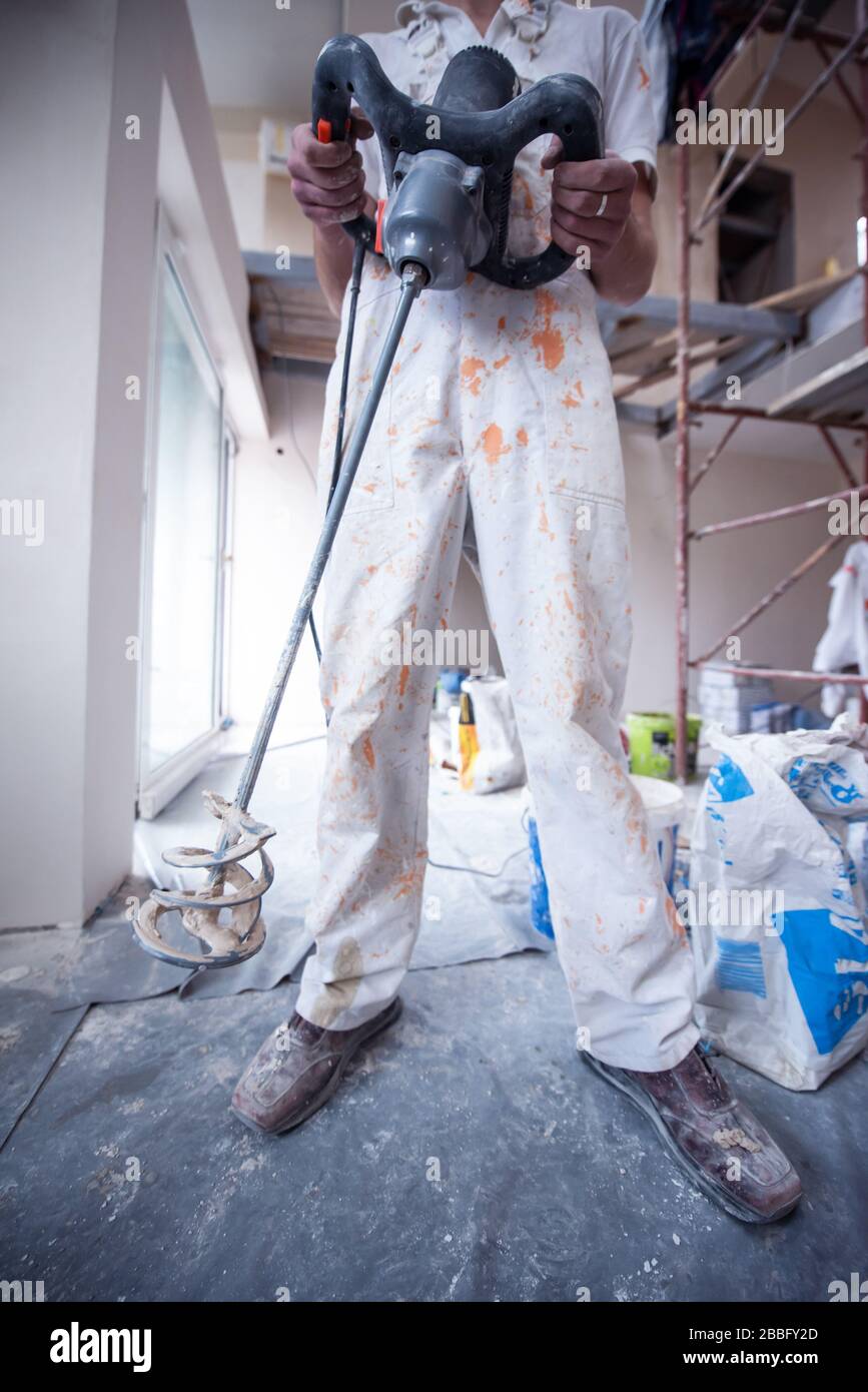 professional Male builder mixing plaster in bucket using electric mixer ...