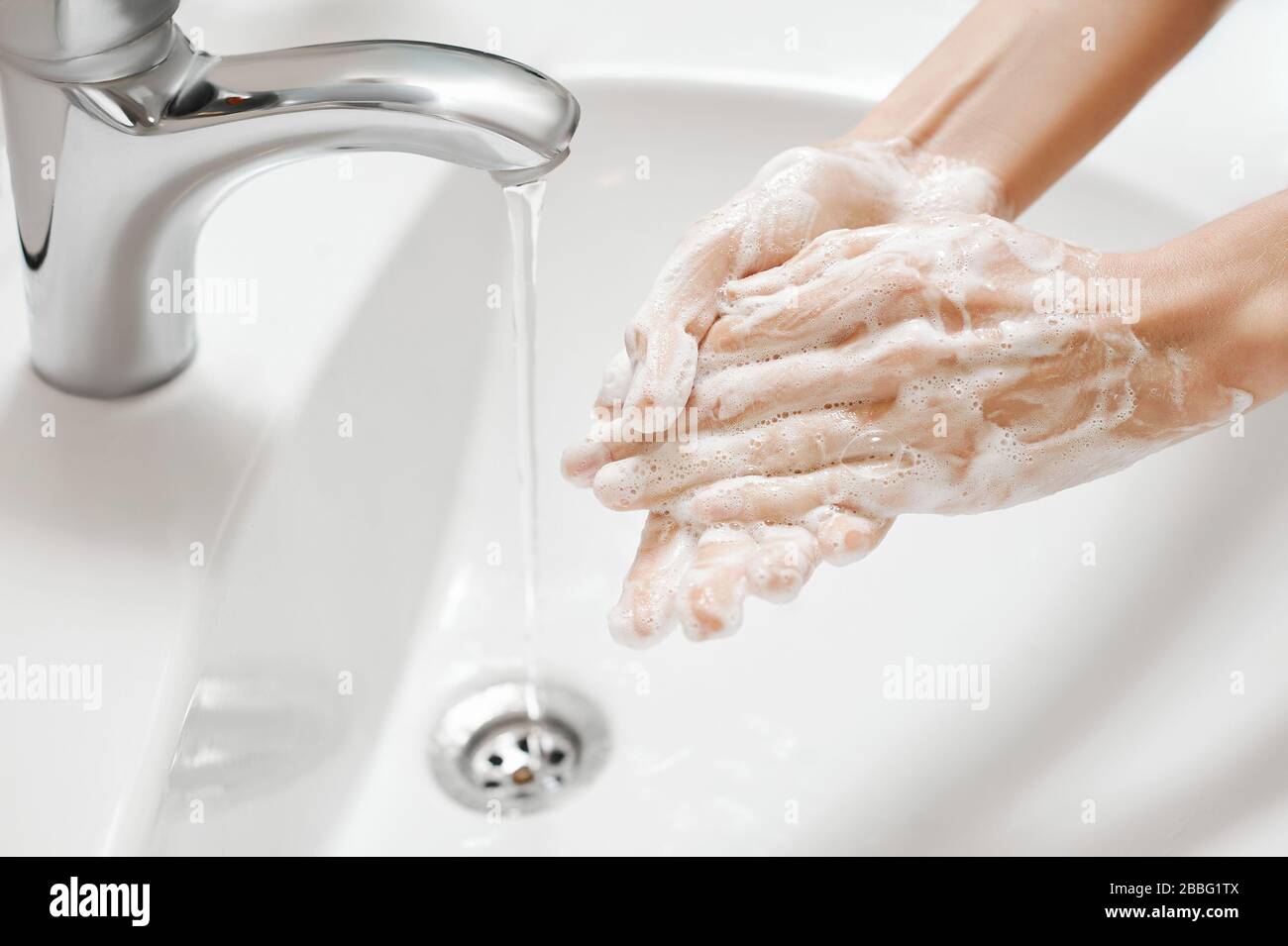 Hand Washing in white sink. Water flows from a faucet at soapy female ...