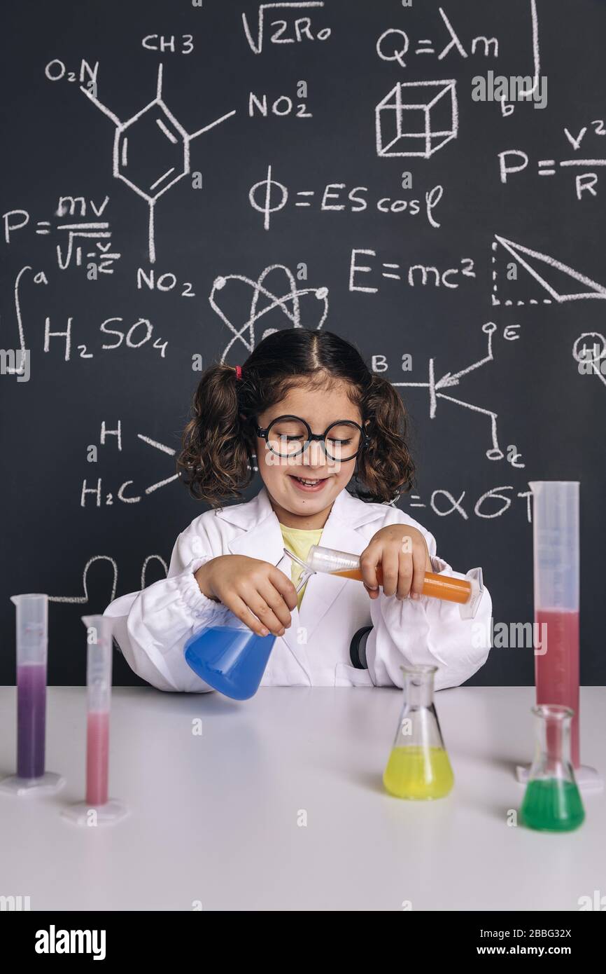 little scientist girl with glasses in lab coat mixing chemical liquids ...