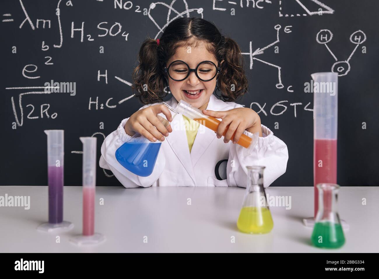 little scientist girl with glasses in lab coat mixing chemical liquids ...