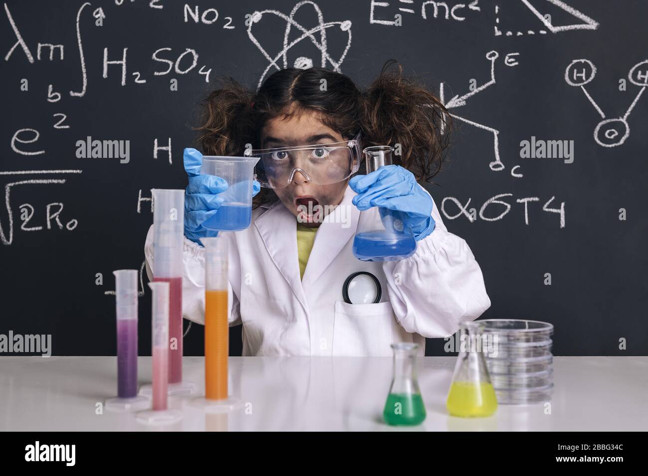 surprised scientist girl with gloves and goggles in lab coat with ...